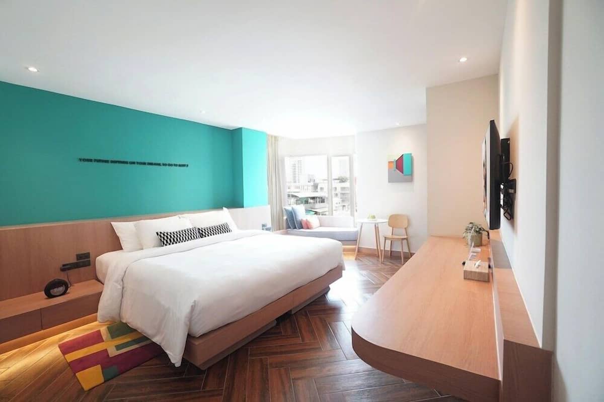 Quarto de hotel moderno com cama, escrivaninha, televisão e vista para a cidade.