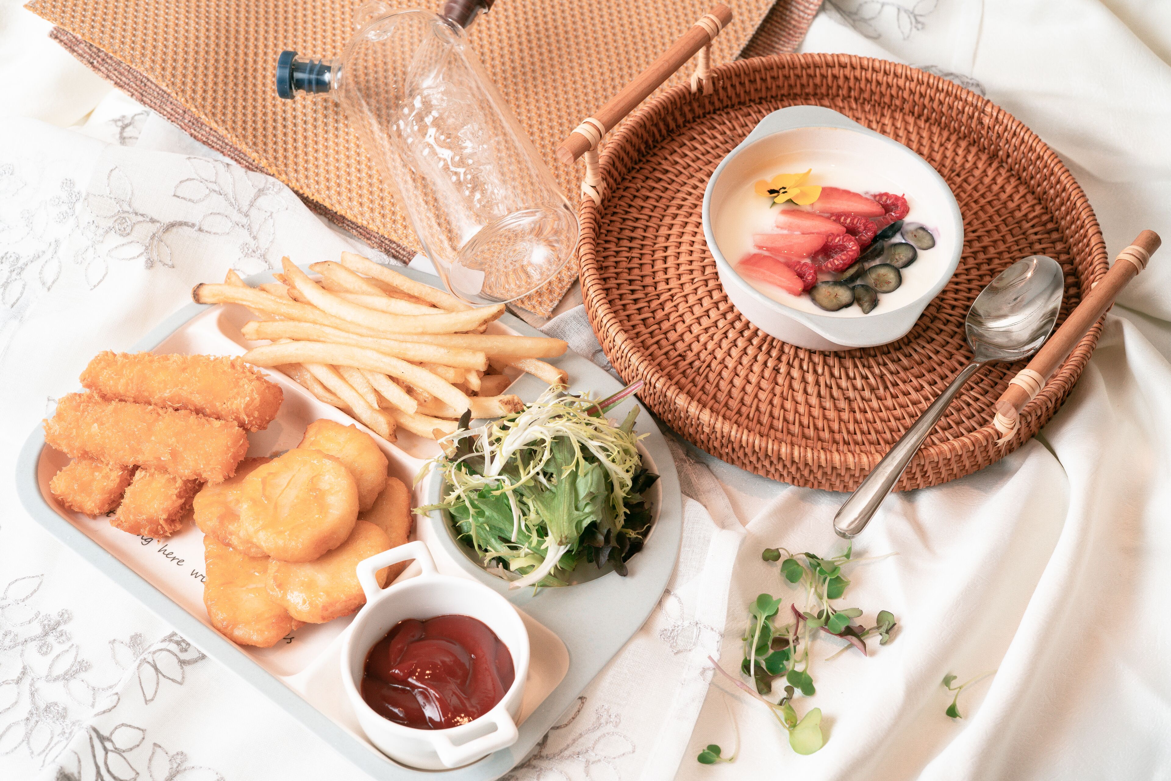 Uma mesa com diversos alimentos, incluindo batatas fritas, peixe empanado, salada e uma tigela de iogurte com fruta.