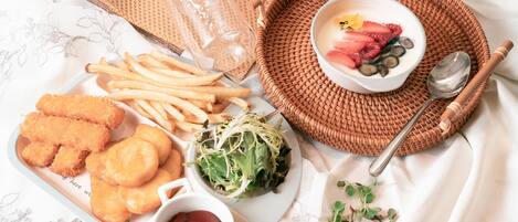 Uma mesa com diversos alimentos, incluindo batatas fritas, peixe empanado, salada e uma tigela de iogurte com fruta.