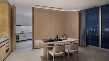Uma sala de jantar moderna com uma mesa e cadeiras de mármore, vista da cidade à noite e uma cozinha ao fundo.