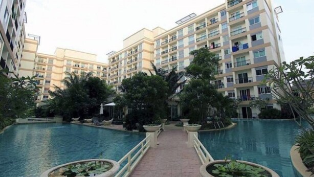 Um edifício residencial com vários andares, com uma piscina central, cercado por vegetação exuberante e palmeiras.