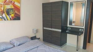 Quarto com cama, guarda-roupa, mesa de cabeceira com luminária e espelho.