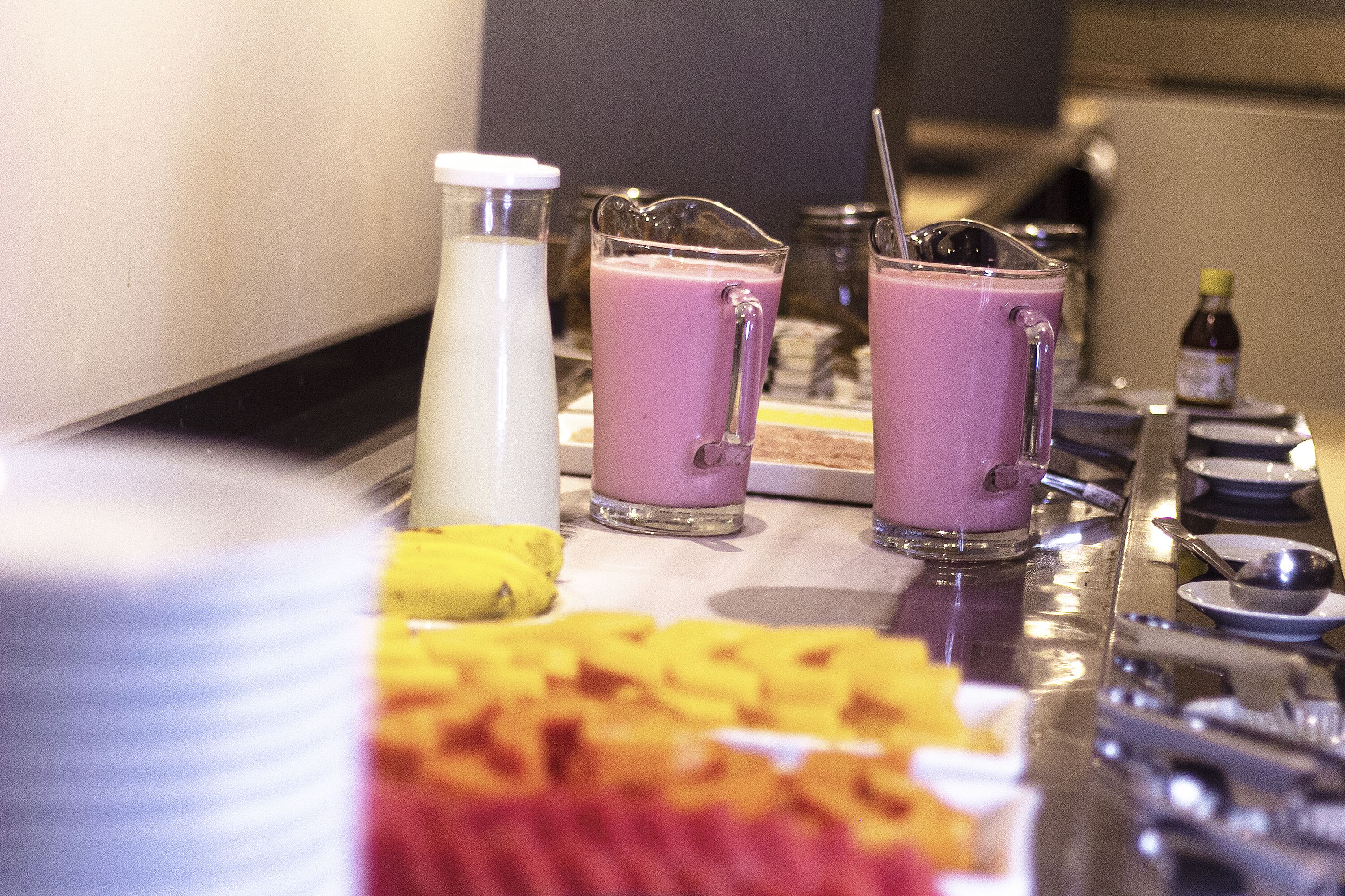 Uma área de buffet com diversos alimentos e bebidas, incluindo um jarro de uma bebida roxa e uma garrafa de leite.
