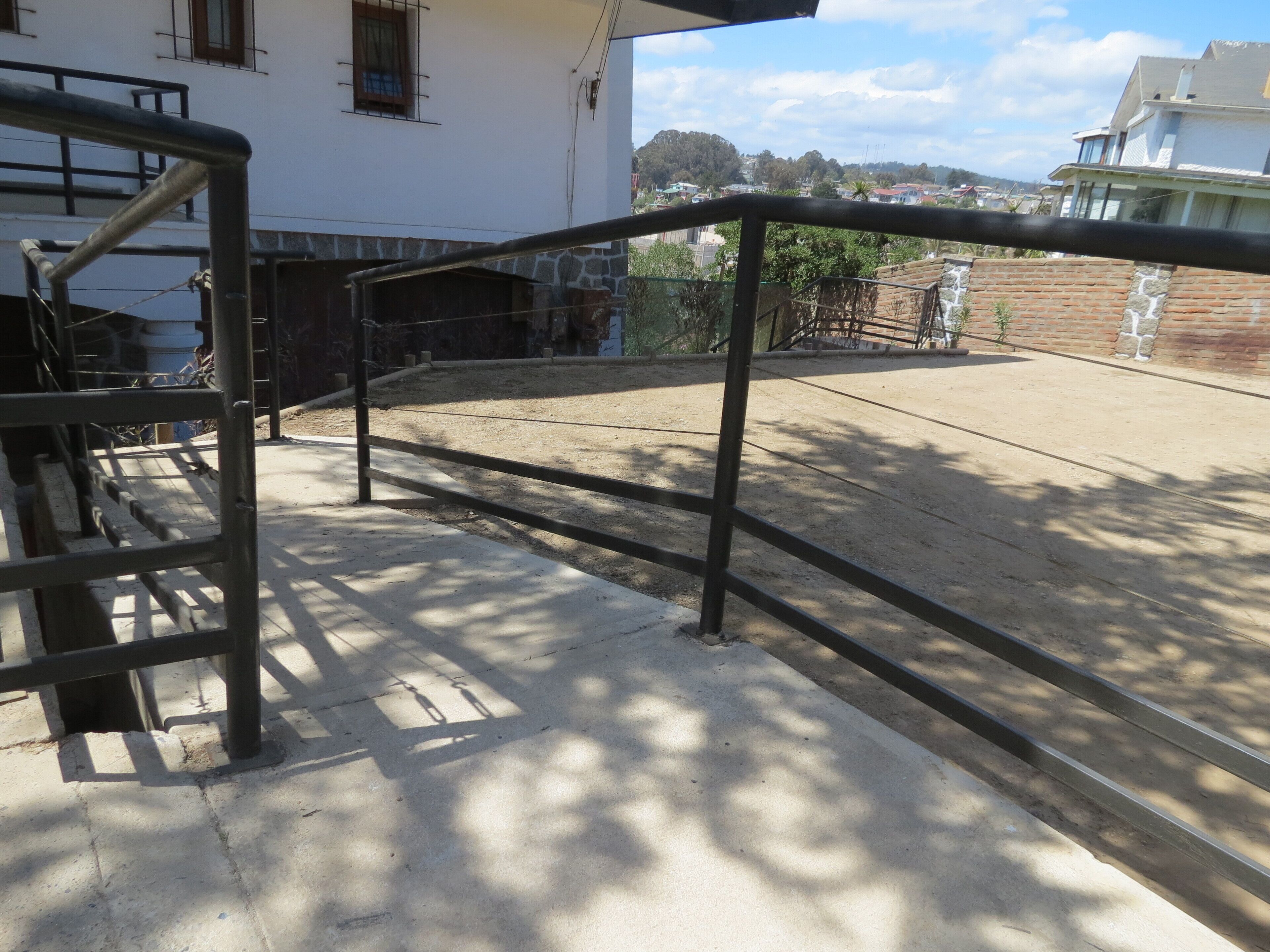 Uma área externa de concreto com grades de metal, uma escadaria e um edifício ao fundo.