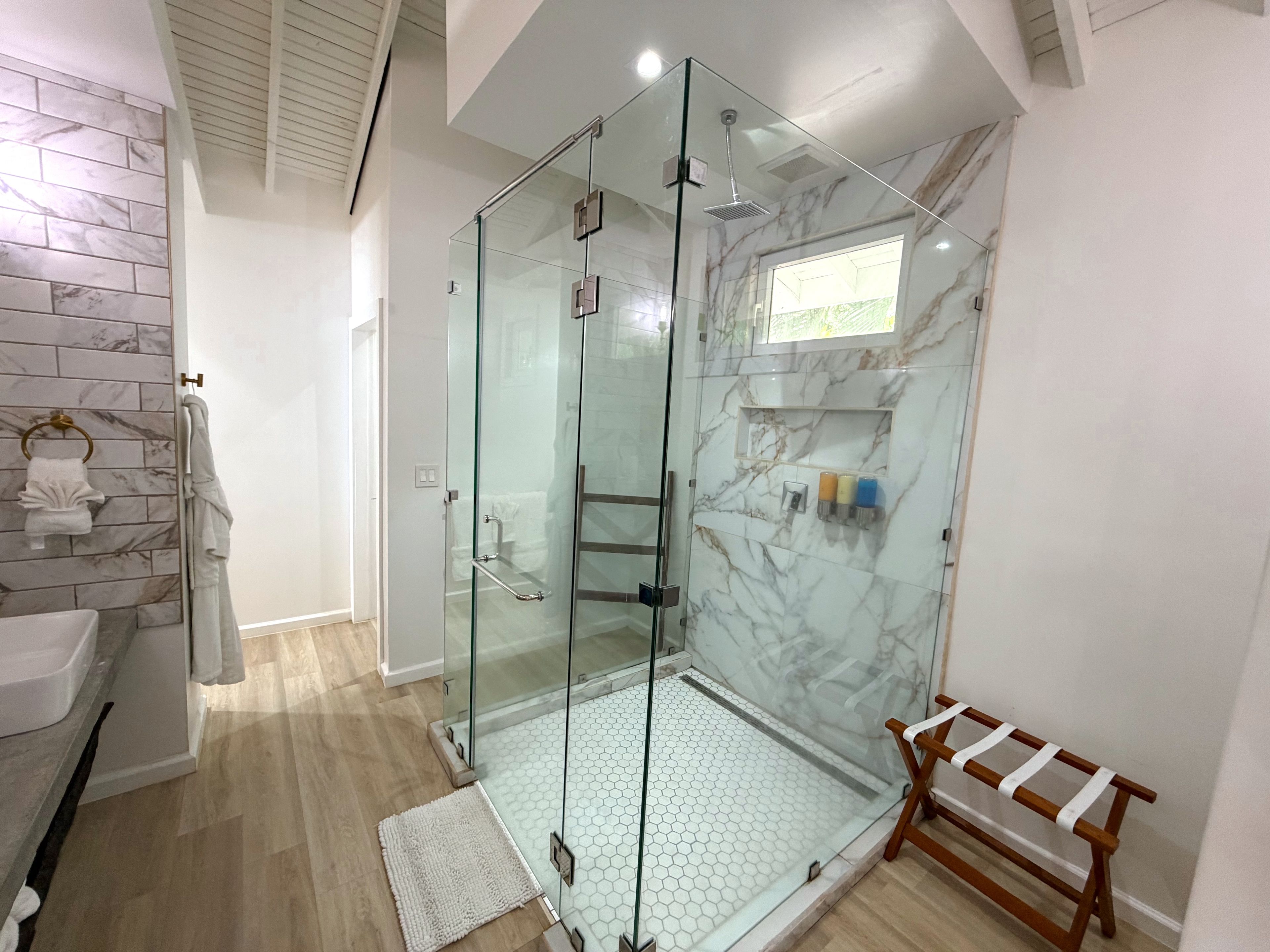 Um banheiro moderno com chuveiro em cabine de vidro, paredes de mármore e um banco de madeira.