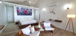 Quarto moderno com cama, área de estar com mesa e uma janela grande com vista.