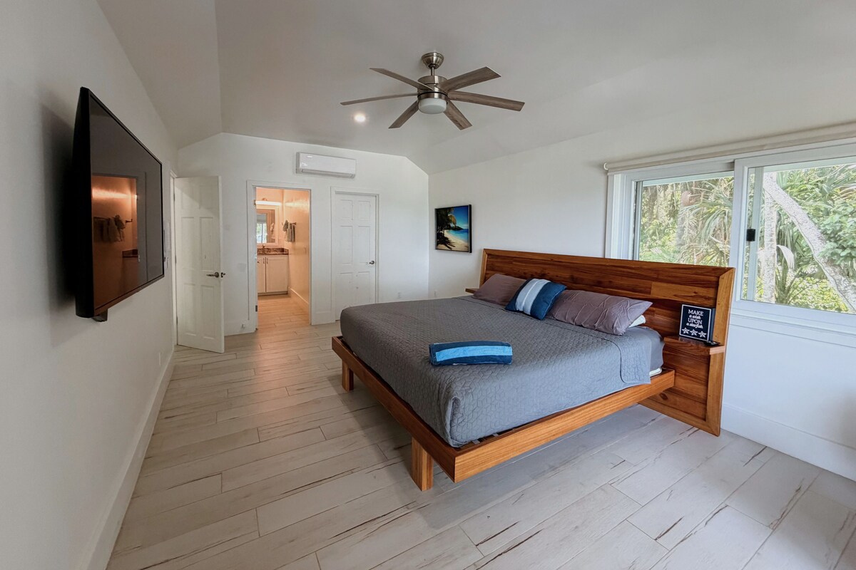 Quarto com cama, ventilador de teto, janela com vista e porta que dá para um banheiro.