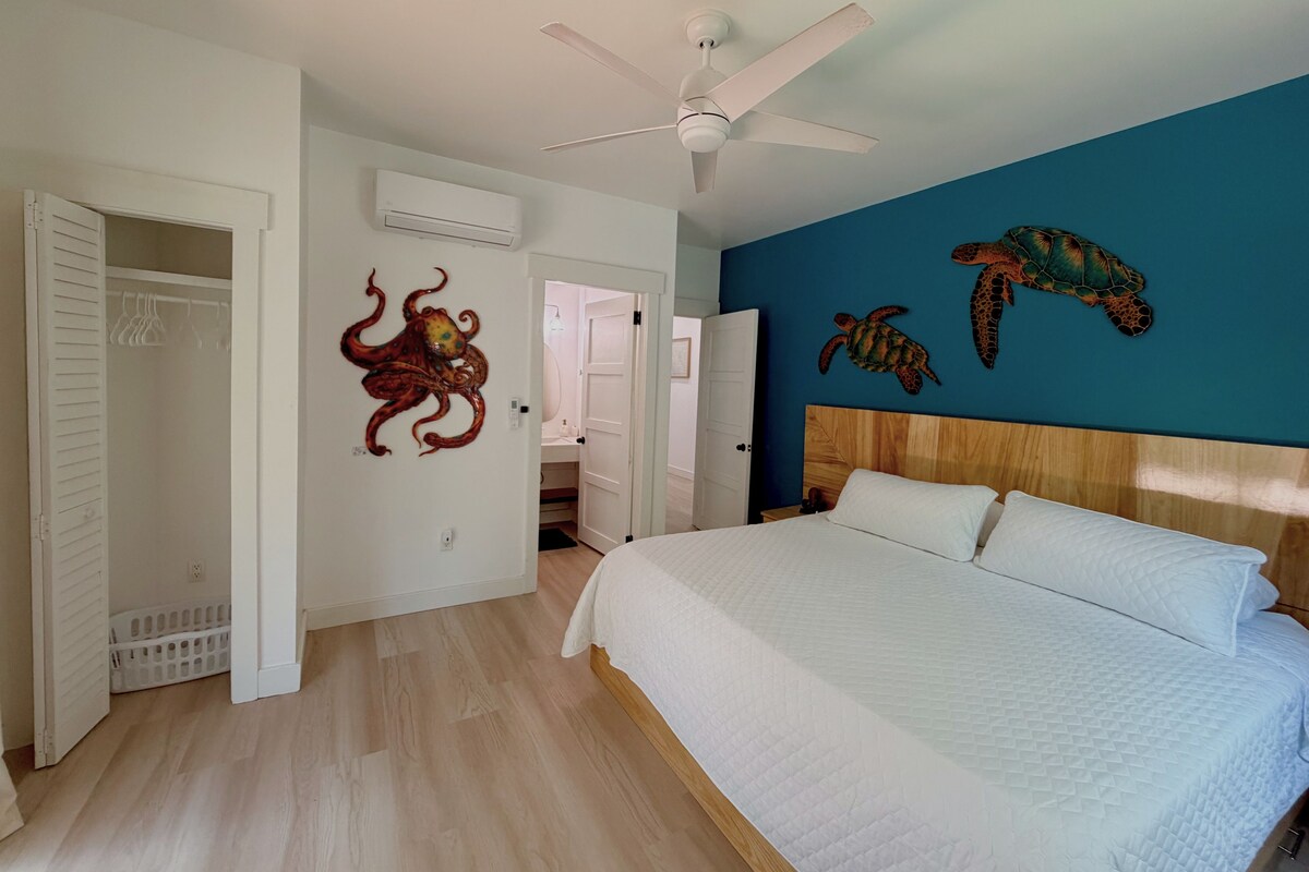 Quarto com cama, ventilador de teto, ar condicionado e parede decorada com um desenho de tartaruga.