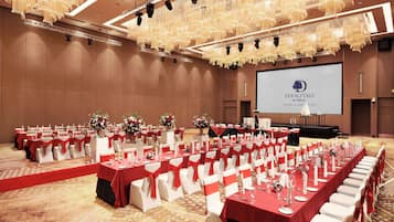 Salão de festas com fileiras de mesas montadas para um evento formal, uma grande tela exibindo o logotipo da DoubleTree by Hilton e um palco com um púlpito.