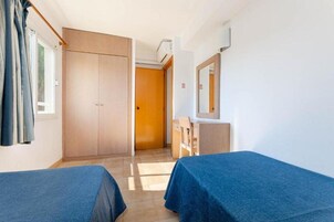 Quarto com duas camas, um guarda-roupa, um espelho e a porta do banheiro.
