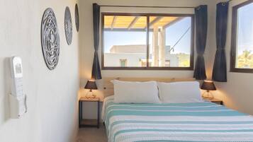 Quarto com cama, duas mesas de cabeceira, janela com cortinas e detalhes na parede.