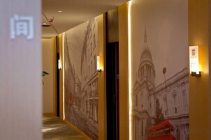 Corredor com um mural mostrando um edifício, um ônibus vermelho e uma porta com interruptor de luz.