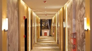 Um corredor de hotel com piso de mármore, luminárias na parede e um objeto vermelho ao fundo.