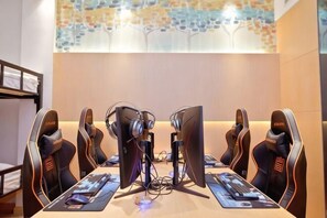 Uma sala de conferências com seis cadeiras de jogos, dois monitores e uma mesa grande.