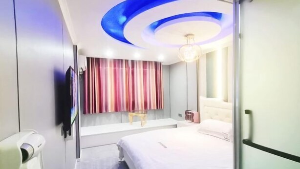 Quarto de hotel moderno com cama, TV fixada na parede e teto com iluminação azul.