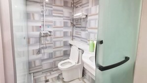 Casa de banho com chuveiro, sanita e porta de vidro.