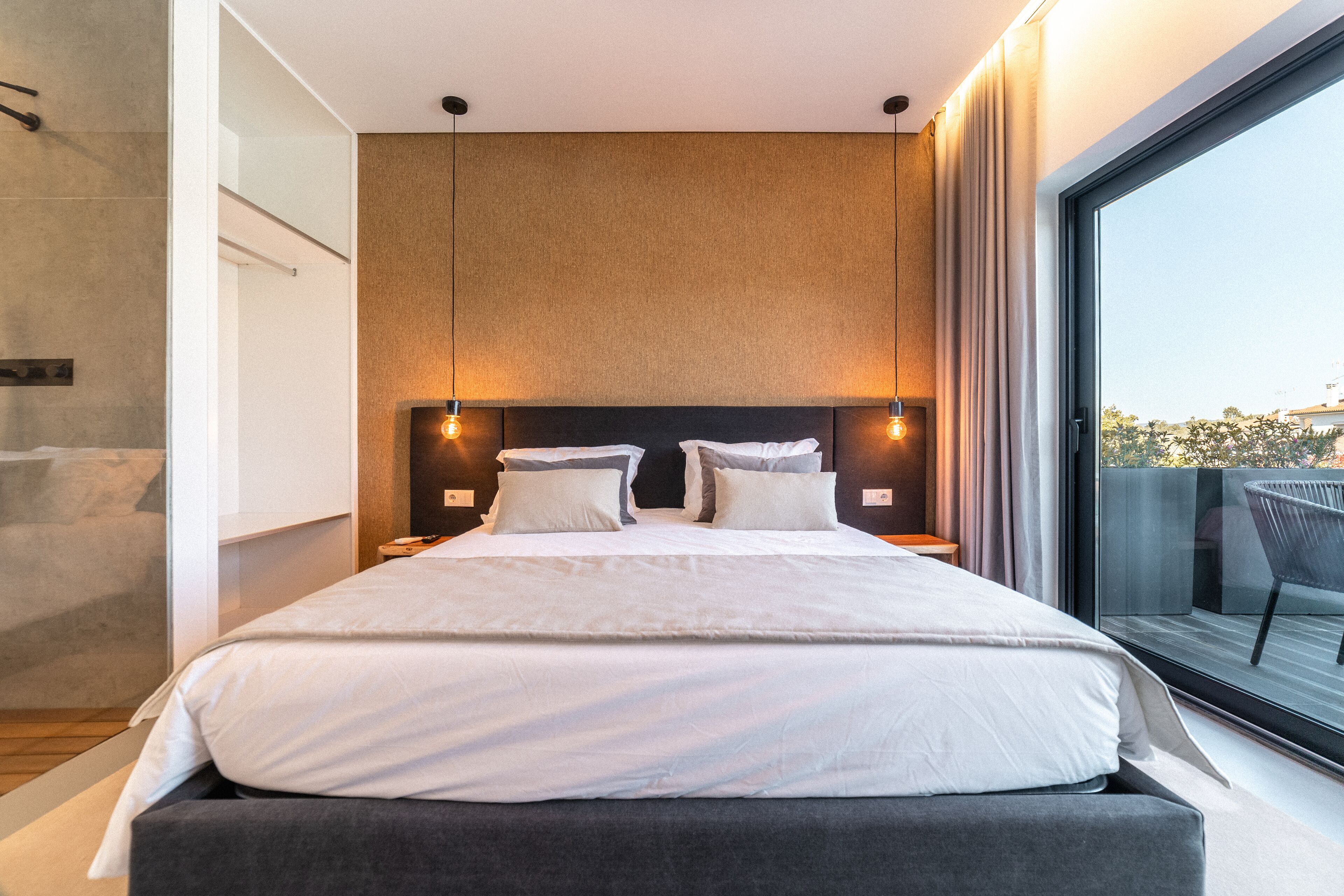 Um quarto moderno com uma cama grande, duas mesinhas de cabeceira e vista para o exterior através de uma grande janela.