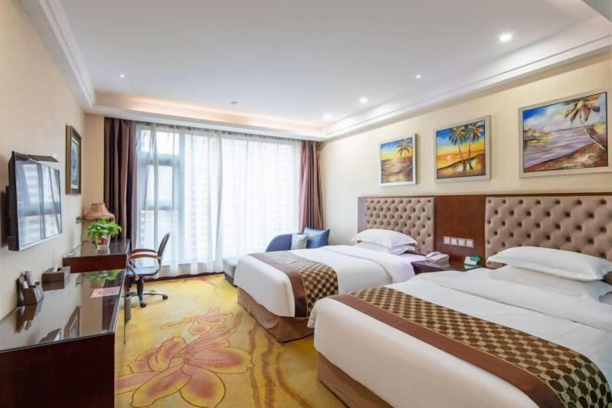 Quarto de hotel com duas camas, uma escrivaninha, uma cadeira e obras de arte nas paredes.