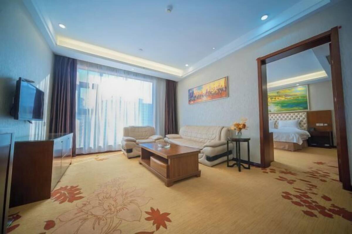 Quarto de hotel com sofá, poltrona, mesa de centro e televisão.