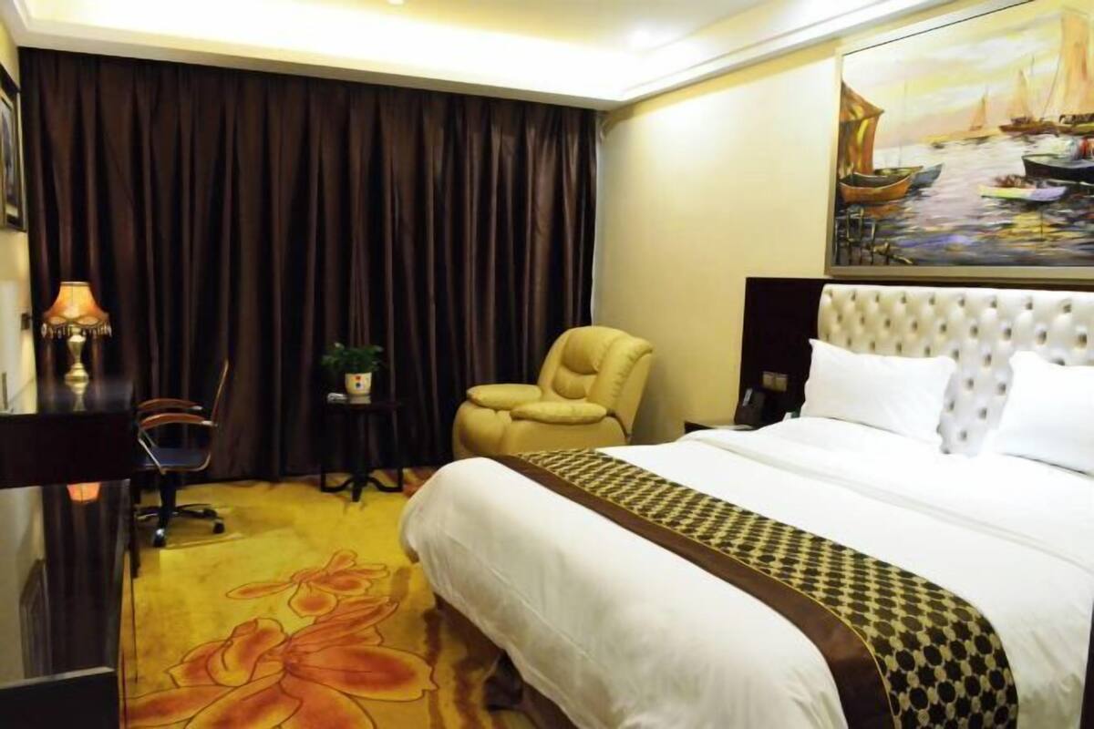 Quarto de hotel com uma cama grande, uma cadeira, uma escrivaninha e um quadro na parede.