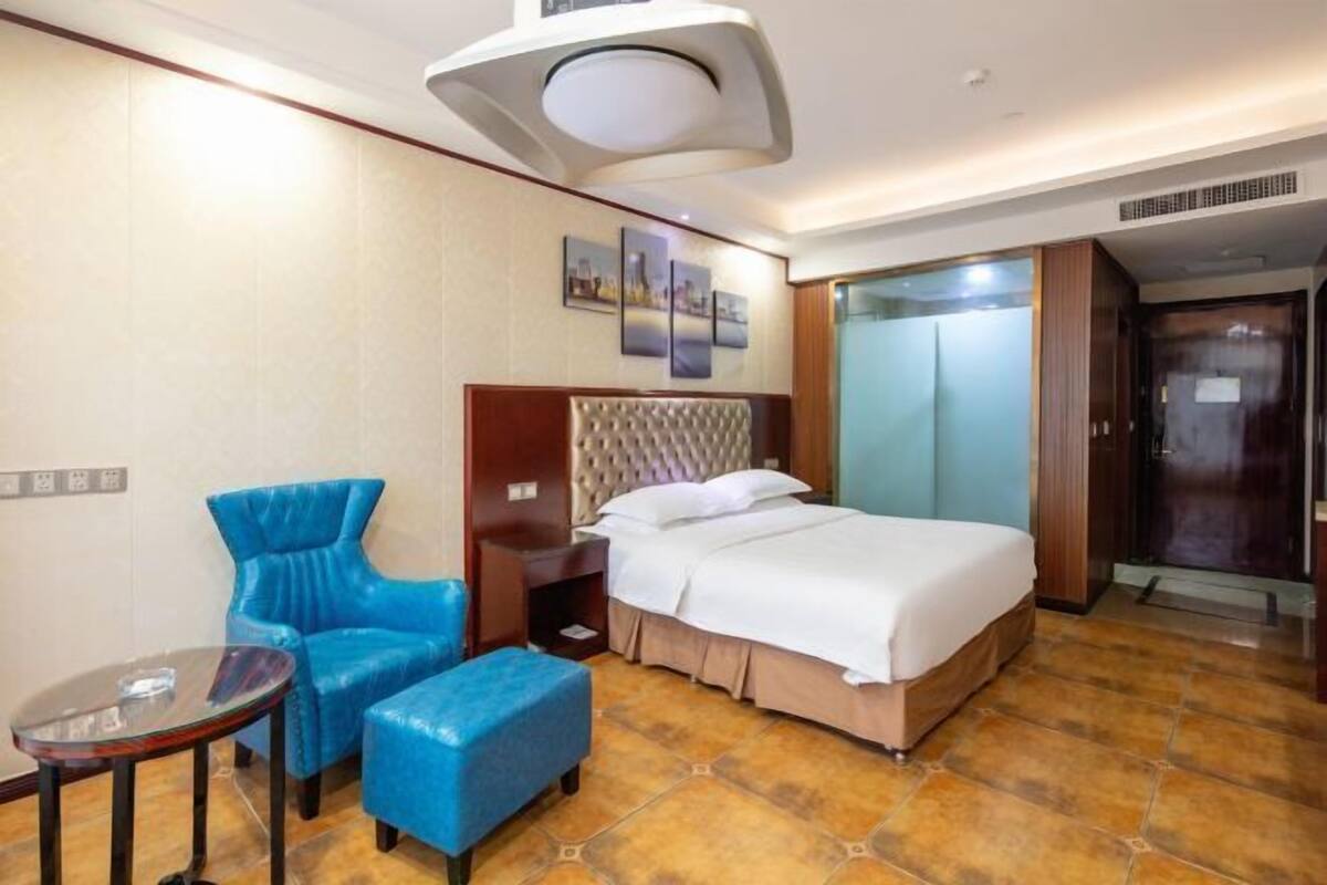 Quarto de hotel com uma cama, uma poltrona azul, uma mesinha e um guarda-roupa.