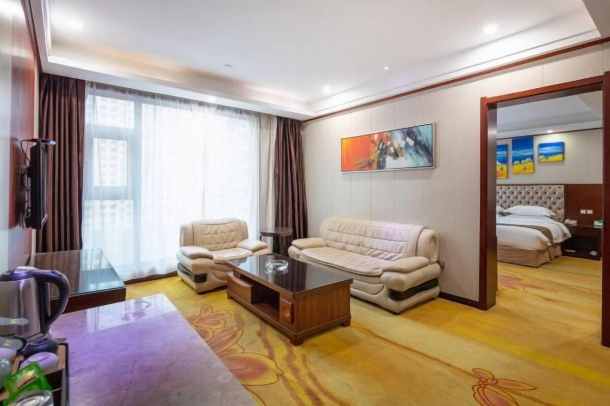 Quarto de hotel com sofá, poltrona, mesa de centro e uma cama.