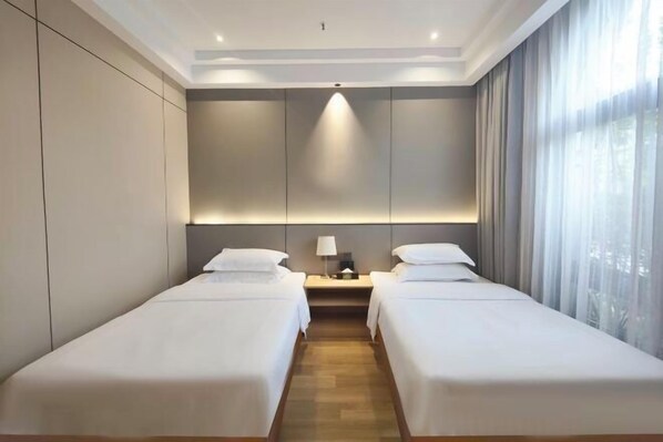 Quarto de hotel com duas camas de solteiro, mesa de cabeceira com abajur, janela grande com cortinas e design moderno no teto.