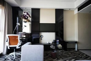 Quarto de hotel moderno com uma cama grande, uma escrivaninha, uma cadeira e uma pequena mesa com abajur.