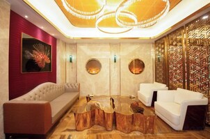 Quarto luxuoso com mesa redonda, sofás brancos, parede de destaque vermelha e lustre.