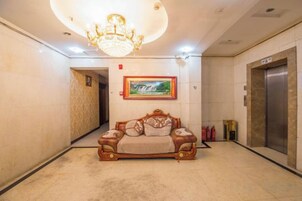 Um hall de entrada com um candelabro, um sofá, um elevador e um quadro na parede.