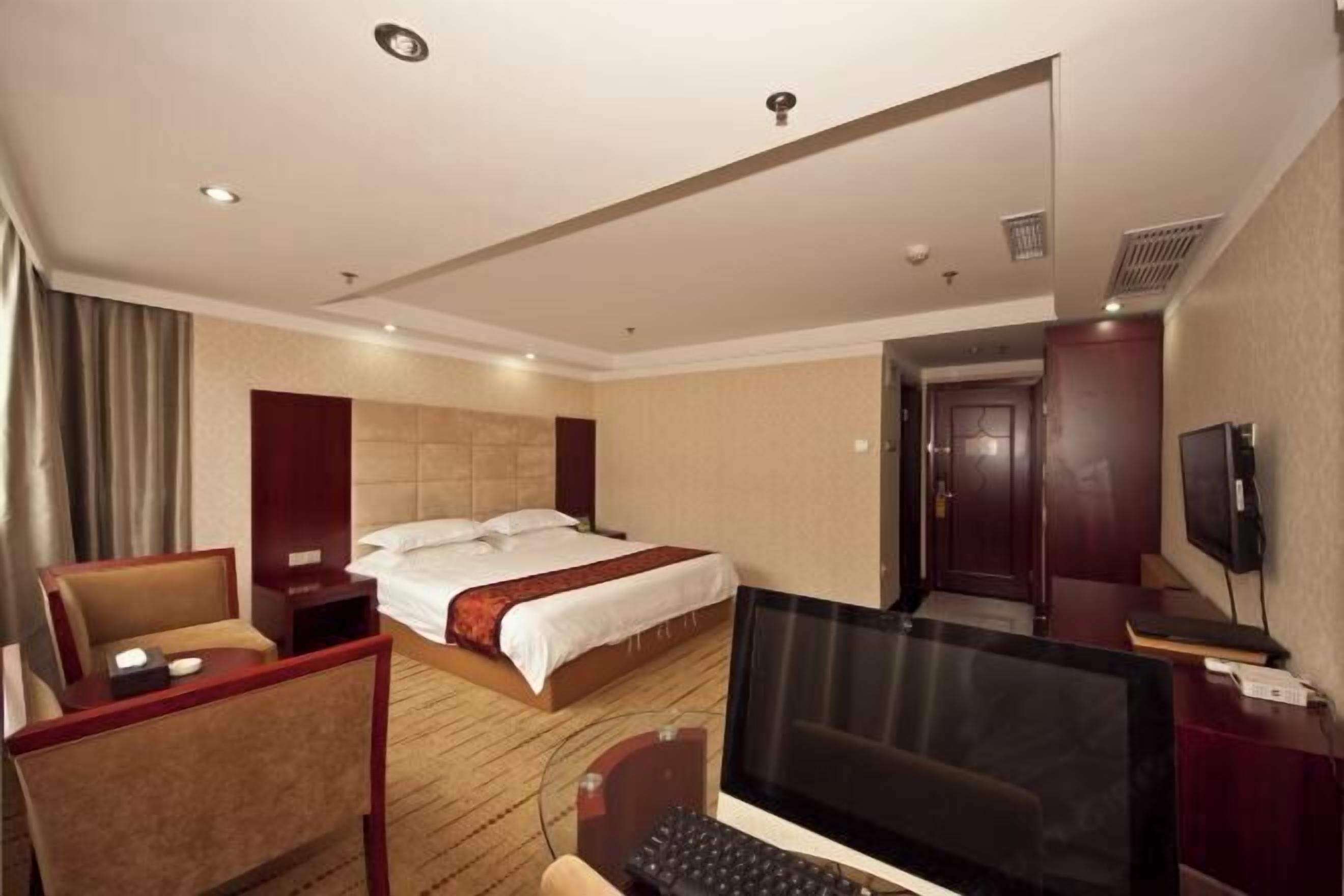 Quarto de hotel com cama, escrivaninha com computador, cadeira e televisão.