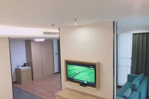 Quarto de hotel com televisão, sofá, escrivaninha e vista para uma paisagem verde.