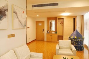 Quarto de hotel com piso de madeira, sofá branco, mesa pequena, cozinha compacta, guarda-roupa e uma tenda infantil.