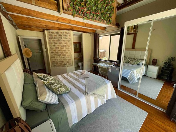 Quarto com cama, escrivaninha, espelho e uma pequena varanda com plantas.