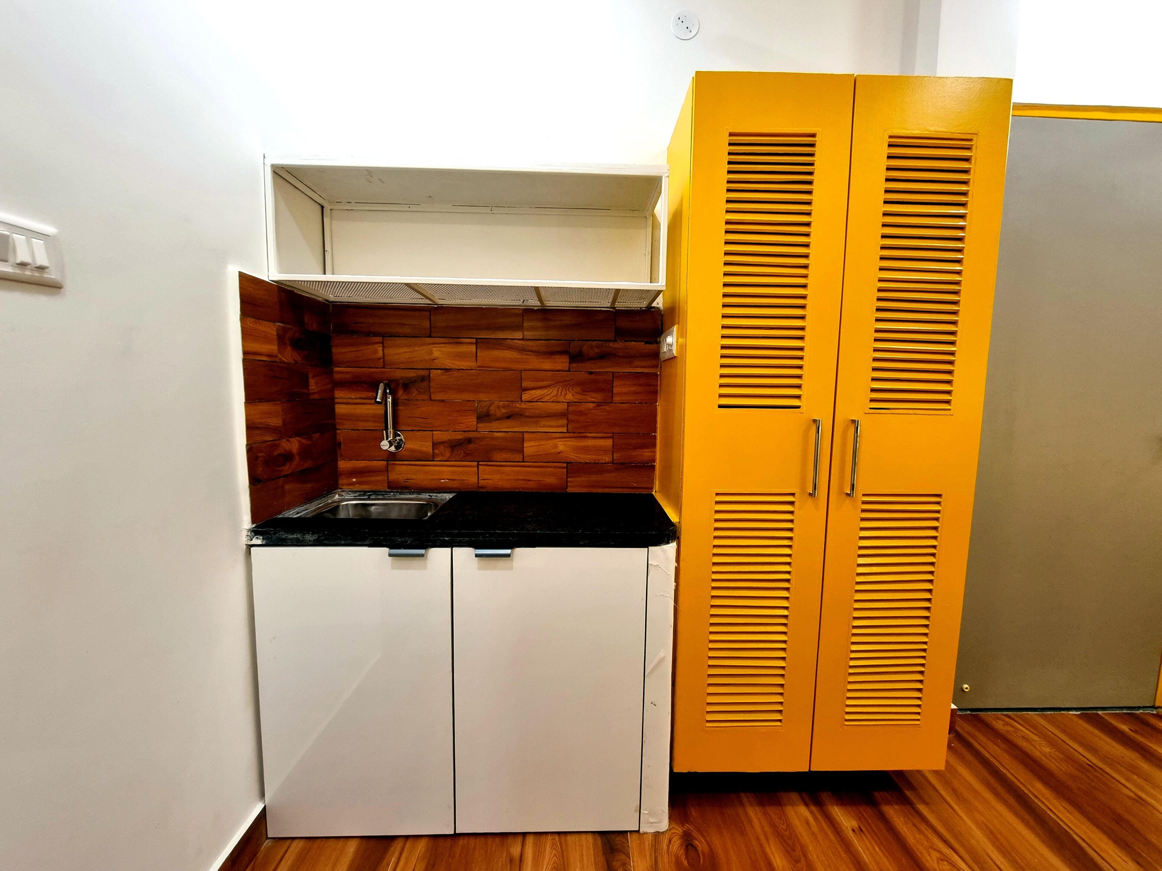 Uma cozinha compacta com pia, painel de madeira e um armário amarelo.