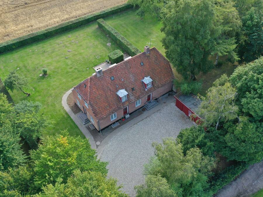 Vista aérea de uma casa tradicional de tijolo com telhado vermelho, rodeada por vegetação exuberante e um gramado bem cuidado.