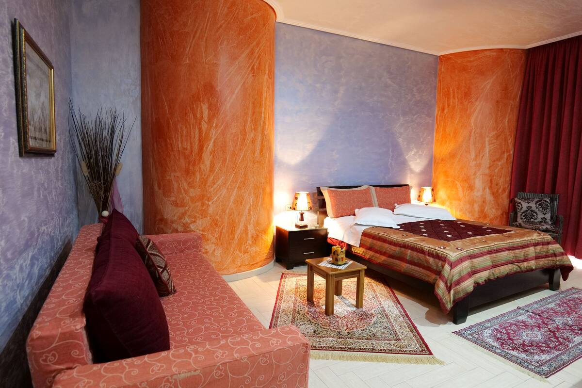 Quarto com cama, sofá, mesa de cabeceira e abajur.
