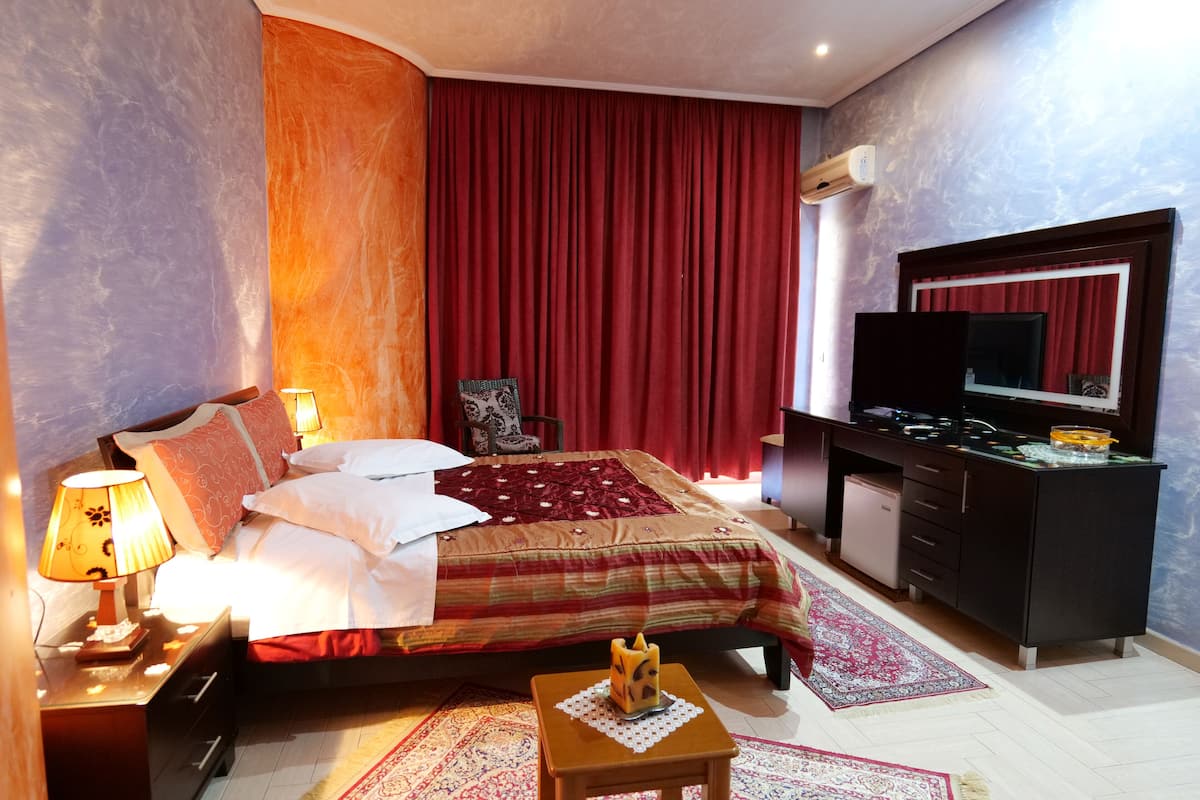 Quarto de hotel com cama, escrivaninha, televisão e uma pequena mesa com um objeto decorativo.