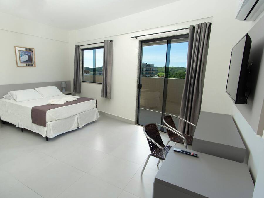 Quarto de hotel com cama, escrivaninha, poltrona, televisão e varanda com vista.