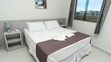 Cama bem arrumada com colcha marrom, abajur e telefone em uma mesinha de cabeceira.