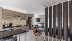 Uma cozinha moderna com bancada preta, uma cadeira colorida e uma mesa de vidro.