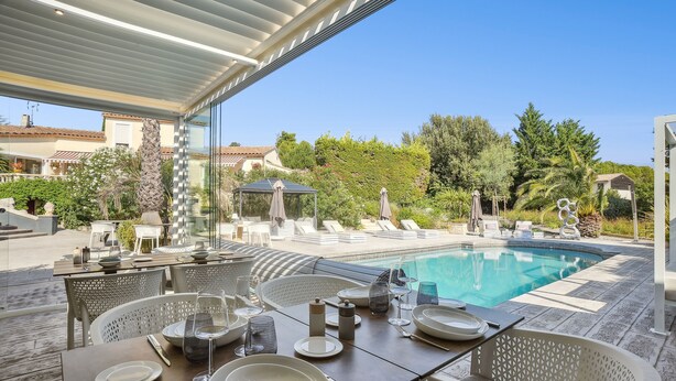 Uma área de refeições com vista para a piscina, mobiliário ao ar livre e um pérgula.