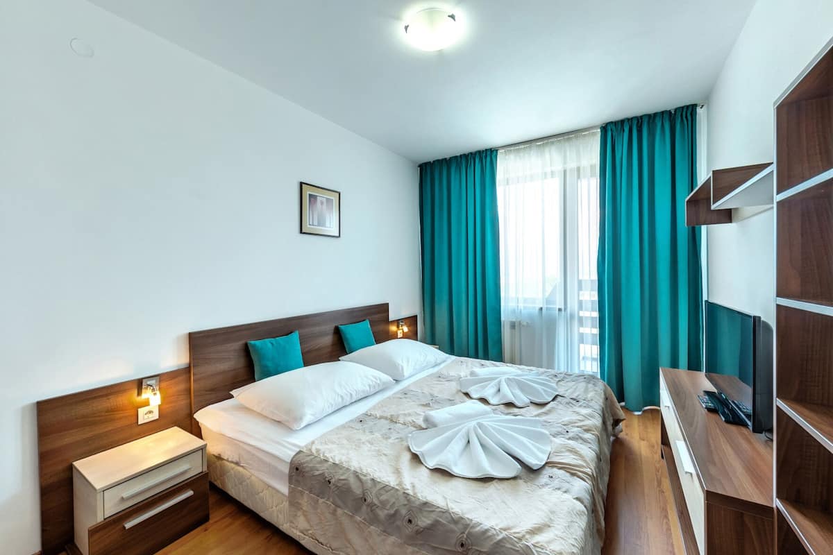 Quarto de hotel moderno com uma cama grande, mesa de cabeceira de madeira, escrivaninha e televisão.