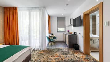 Quarto de hotel com cama, escrivaninha, cadeira, televisão e banheiro.
