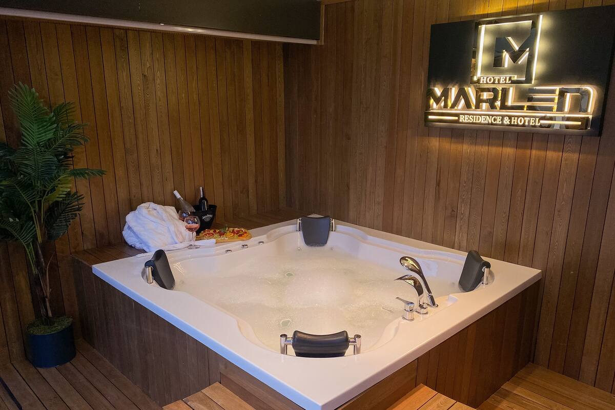 Uma banheira de hidromassagem grande e retangular com interior de madeira e uma placa acima com a inscrição "Marled Residence & Hotel".