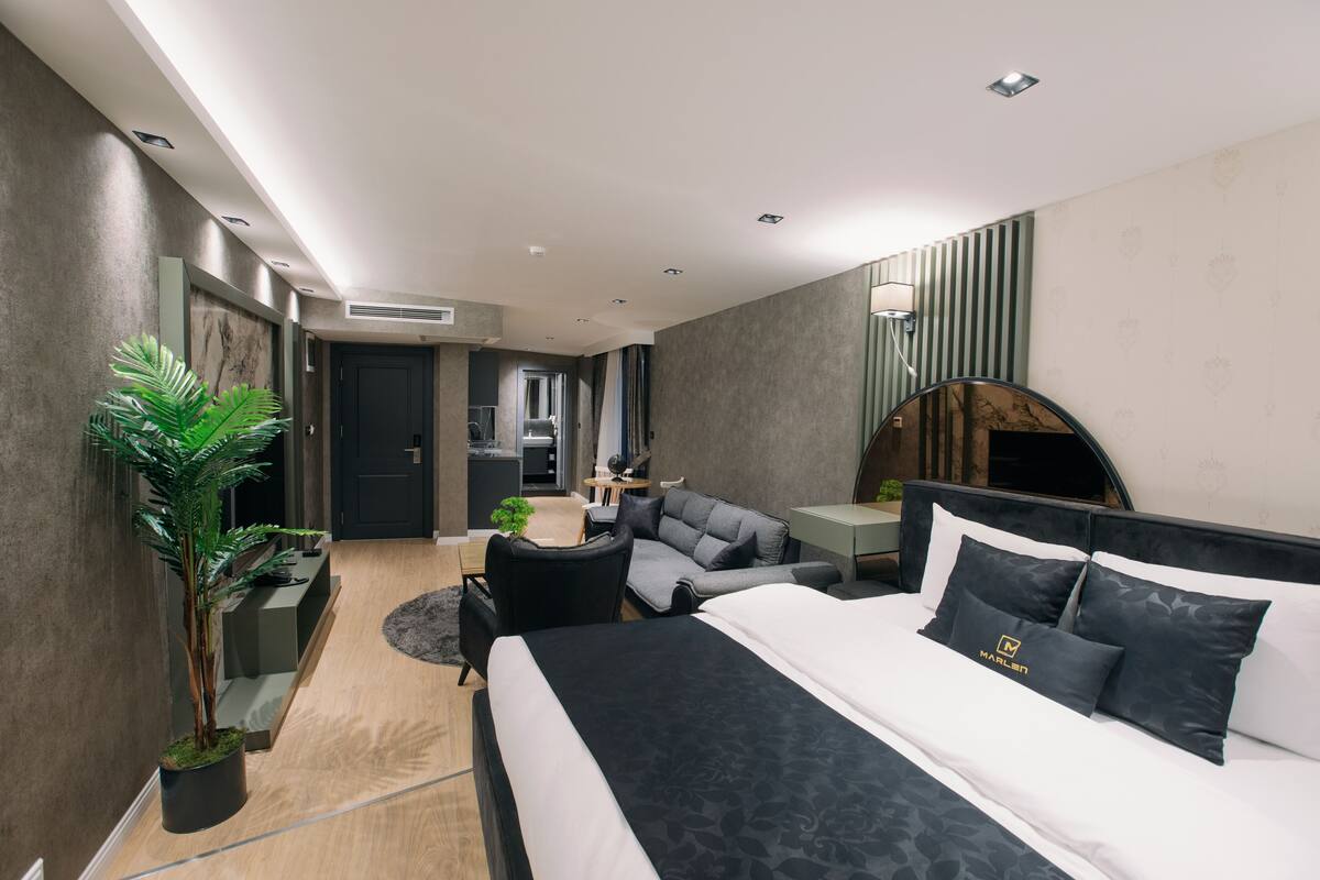 Quarto de hotel moderno com uma cama grande, área de estar, escrivaninha e planta em vaso.
