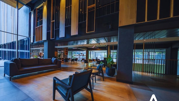 Um hall amplo com design moderno, apresentando uma grande área de estar com sofás e poltronas, uma planta grande em vaso e vista para o exterior através de amplas janelas.