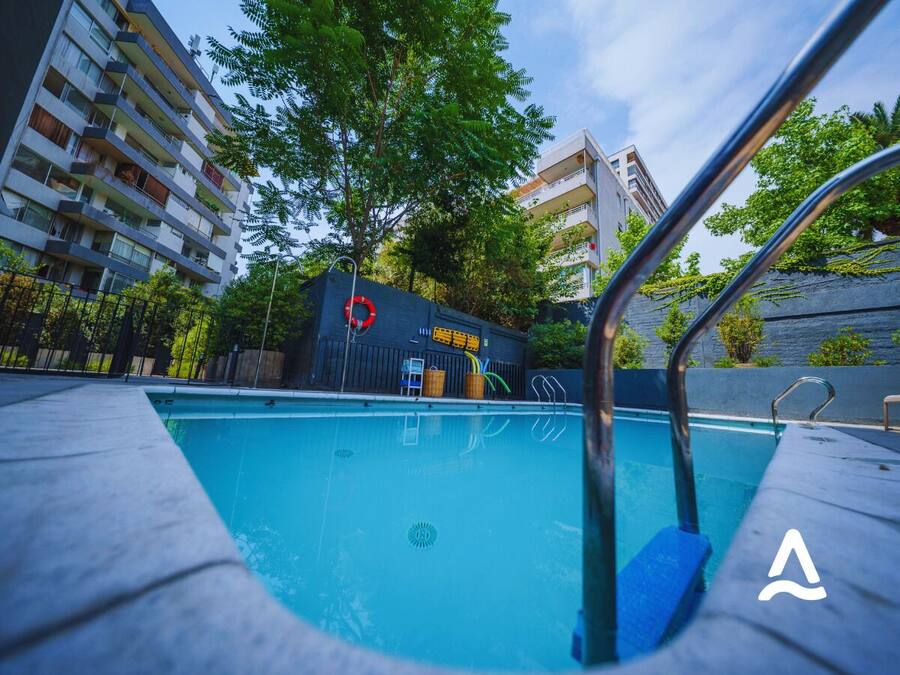 Piscina com boia salva-vidas e placa em idioma estrangeiro, cercada por árvores e um edifício.
