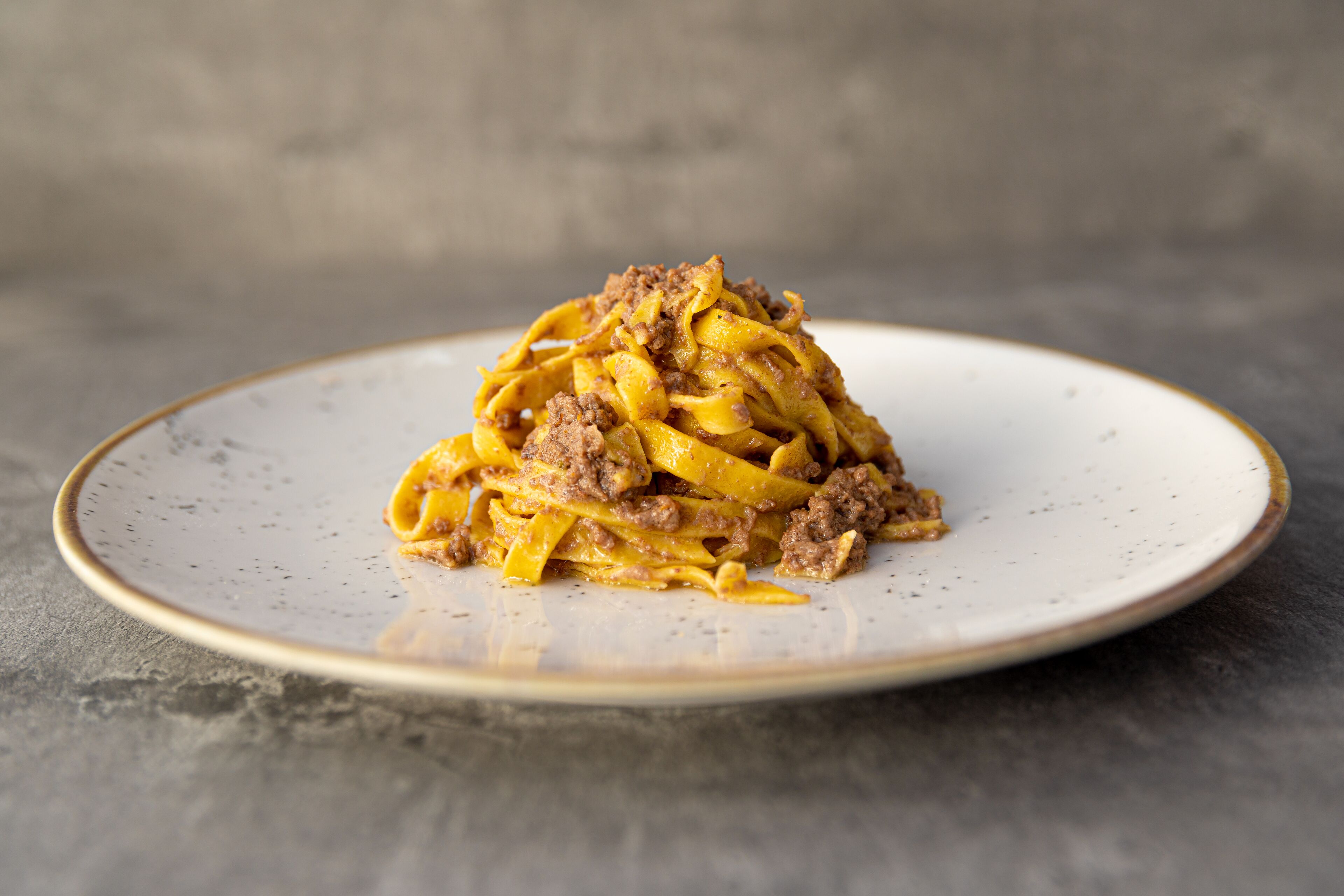 Um prato de massa com carne moída sobre um prato branco simples.