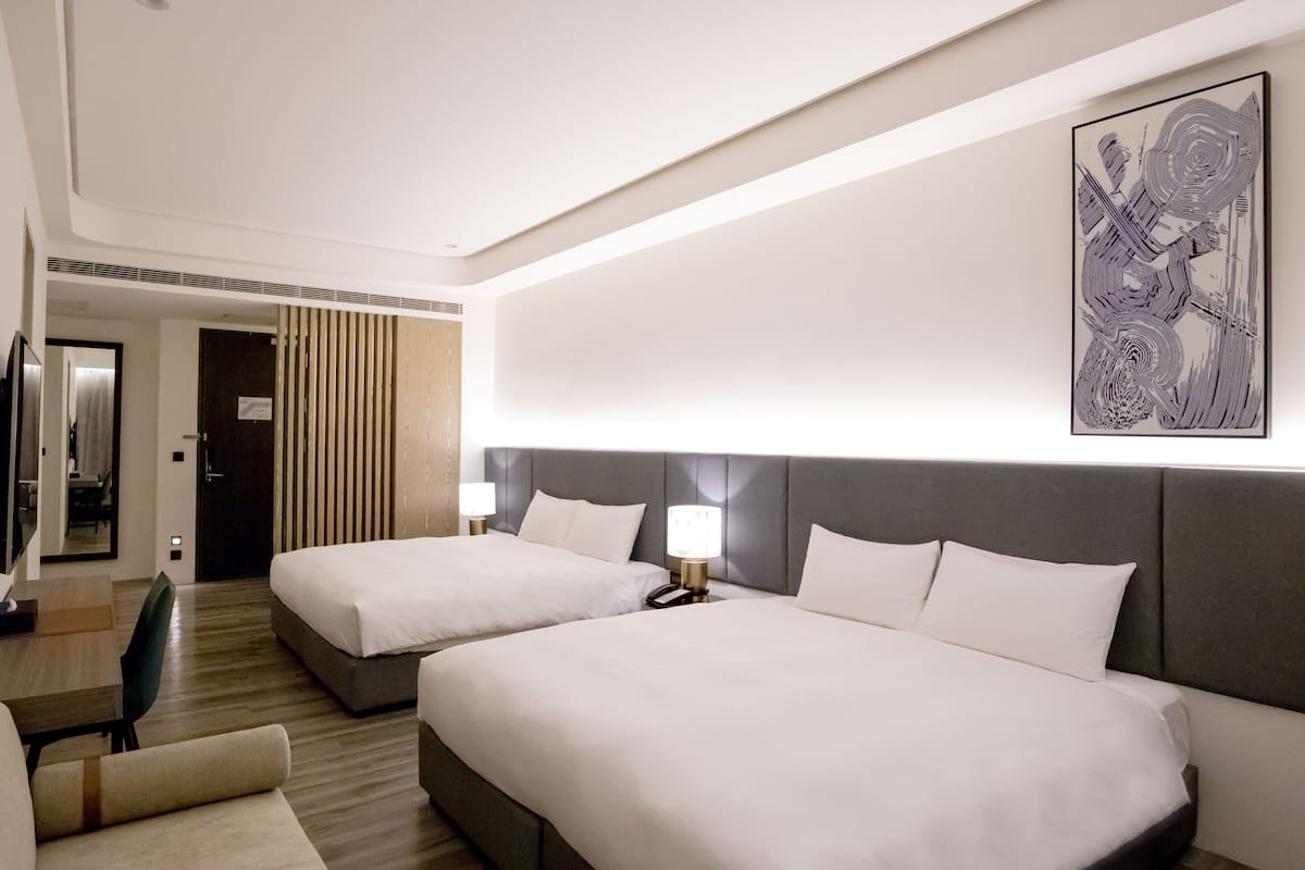 Quarto de hotel com duas camas, uma escrivaninha, uma cadeira e uma grande pintura abstrata na parede.